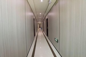 Corredor de hotel comprido e estreito, com portas em ambos os lados e um caminho central.