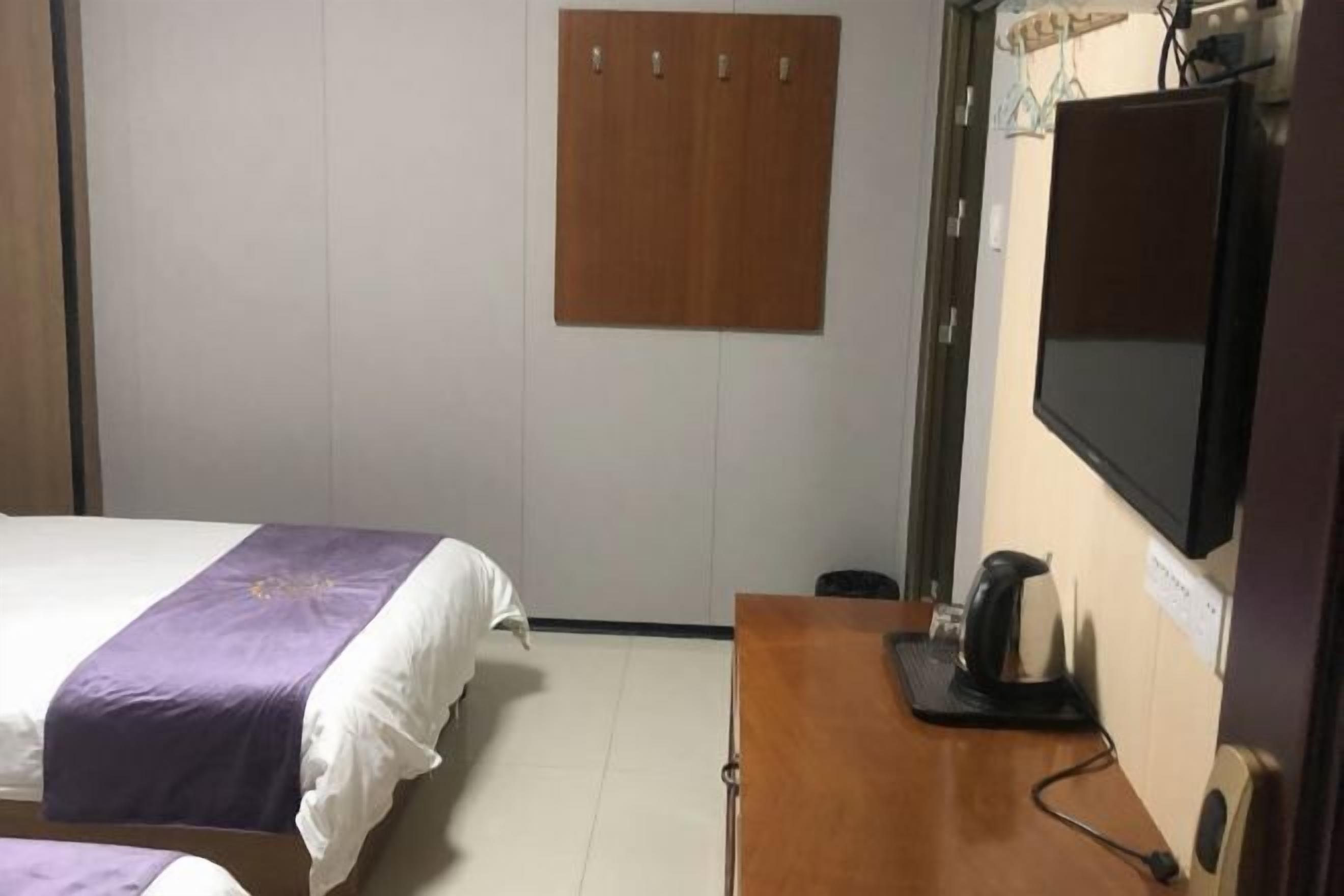 Quarto de hotel com uma cama, uma escrivaninha com computador, televisão e guarda-roupa.