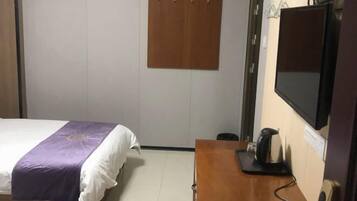 Quarto de hotel com uma cama, uma escrivaninha com computador, televisão e guarda-roupa.
