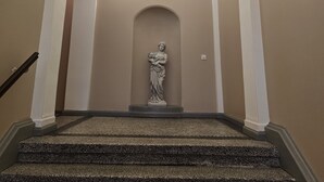 Uma escadaria imponente com design clássico, exibindo uma estátua no topo, colunas brancas e um teto decorativo.