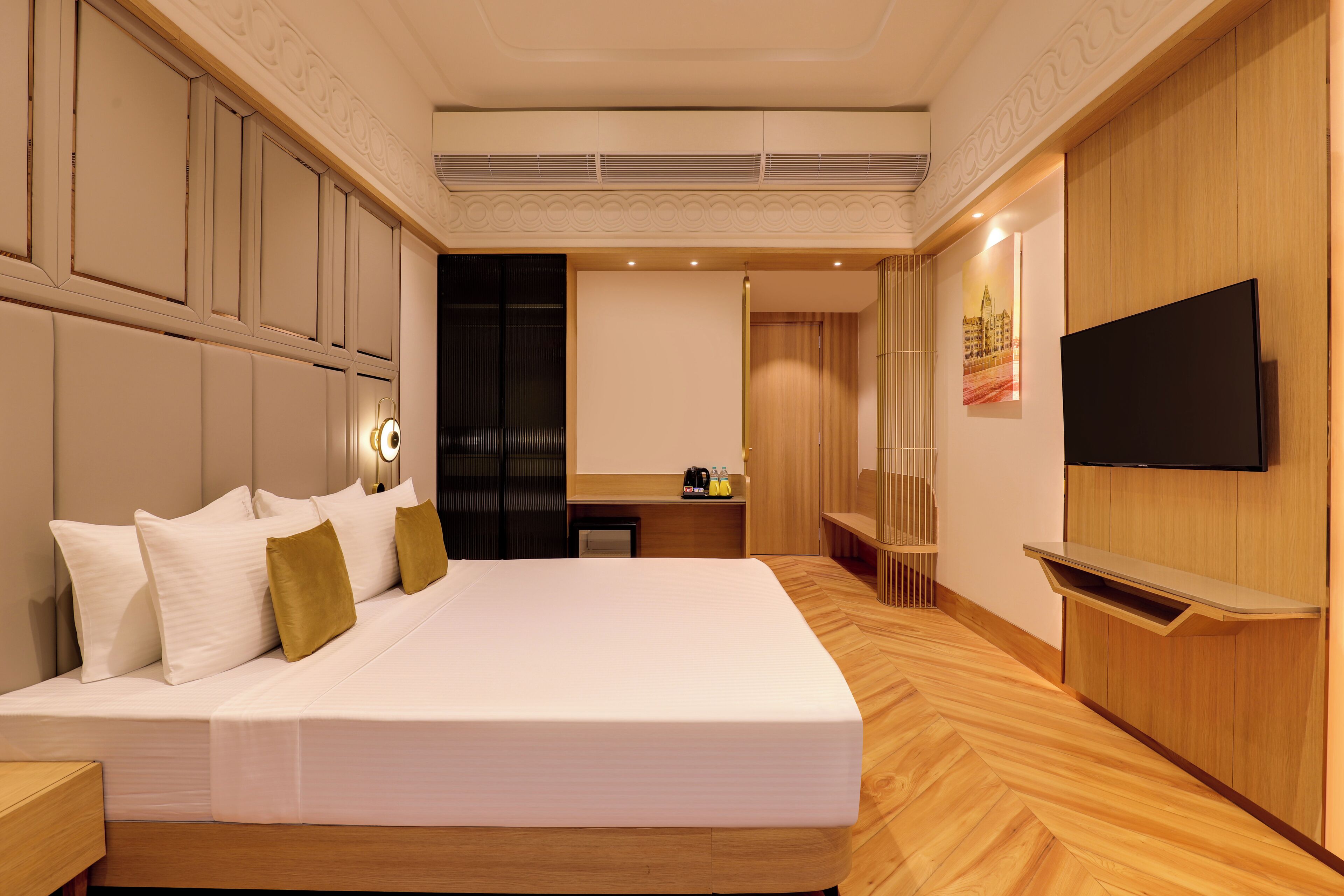 Quarto de hotel moderno com uma cama grande, uma televisão de tela plana na parede, um pequeno kitchenette e piso de madeira.