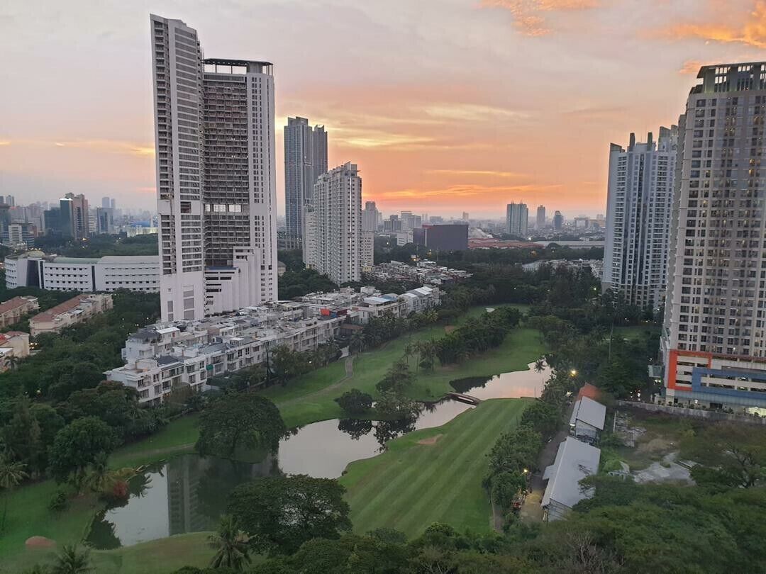 Zona urbana com edifícios altos e modernos, um campo de golfe e um parque com lago.