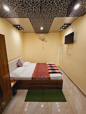 Quarto com uma cama, um ventilador de teto, uma TV e um tapete verde.