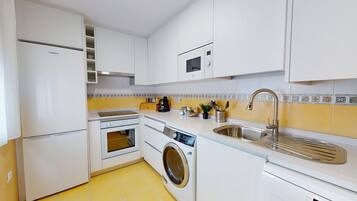 Uma cozinha compacta com armários brancos, micro-ondas embutido, máquina de lavar e pia com torneira moderna.