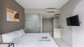 Quarto de hotel moderno com uma cama grande, televisão de tela plana, guarda-roupa e uma pequena cozinha.