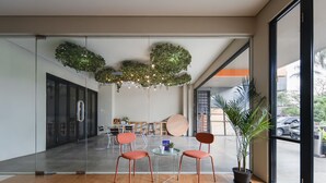 Interior moderno com paredes de vidro, uma mesa redonda, duas cadeiras vermelhas e um vaso com planta.