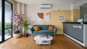 Uma área de recepção moderna com um sofá verde, uma mesa de centro branca e um balcão de recepção com a inscrição 'Cove'.