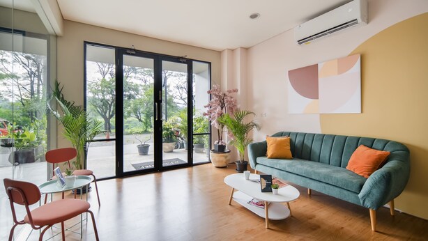 Uma sala de estar moderna com um sofá verde, uma mesa de centro e uma mesa de vidro com cadeiras. Há uma janela grande com vista para árvores e uma porta que dá para o exterior.
