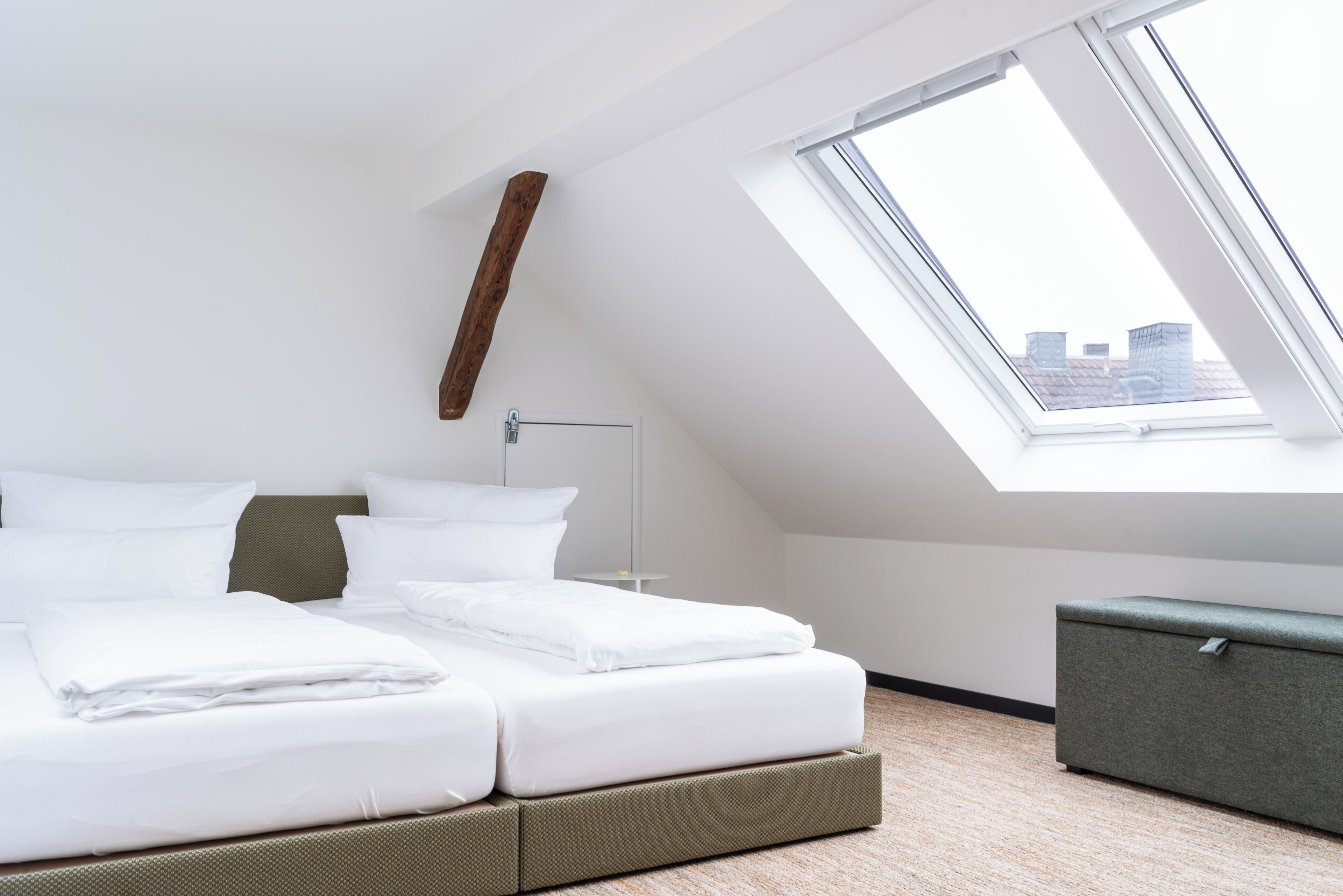 Quarto moderno com claraboia, cama com roupa de cama branca, mesa de cabeceira e um móvel de armazenamento verde.