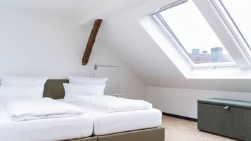 Quarto moderno com claraboia, cama com roupa de cama branca, mesa de cabeceira e um móvel de armazenamento verde.