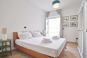 Cama bem arrumada com lençóis e toalhas brancos, um abajur e uma pequena mesa de cabeceira verde.