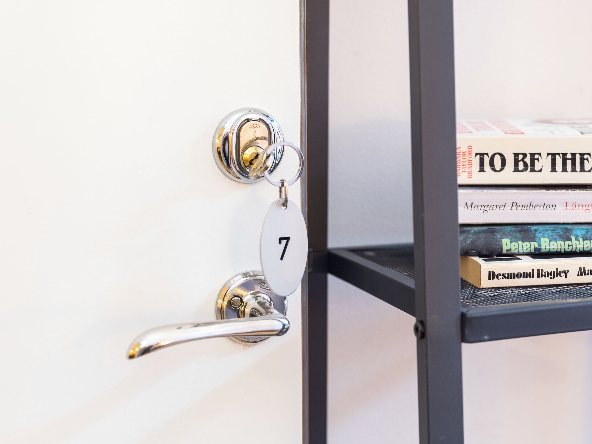 Uma porta com teclado numérico e fechadura, ao lado de uma estante de livros.