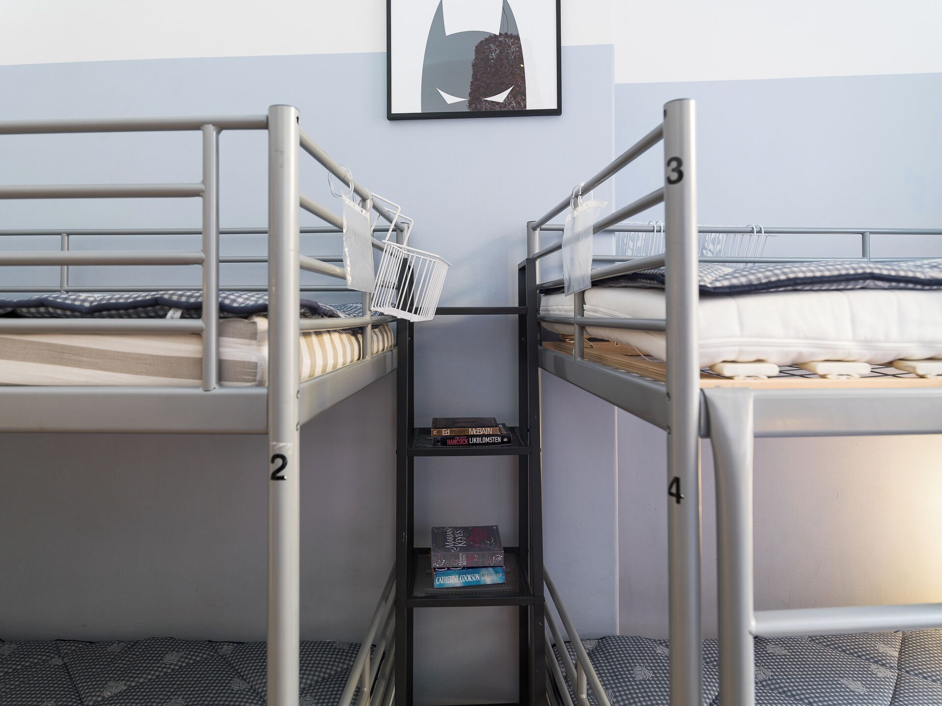 Quarto com beliche, grades de metal, quadro na parede e estante com livros.