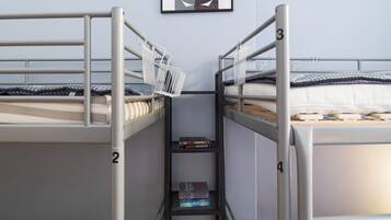 Quarto com beliche, grades de metal, quadro na parede e estante com livros.