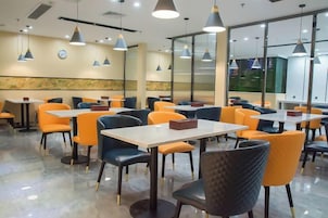 Um restaurante com várias mesas e cadeiras, grandes janelas e iluminação pendente.