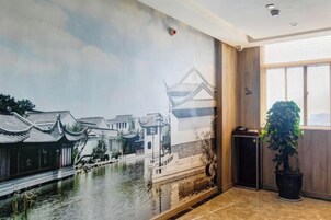Quarto com um mural de arquitetura tradicional, uma planta em vaso e uma janela com persianas.