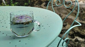 Uma caneca de vidro transparente com um arranjo floral sobre uma mesa de metal verde ao ar livre.