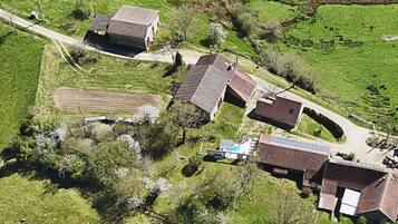 Vista aérea de uma propriedade rural com vários edifícios, incluindo casas e celeiros, rodeada por campos verdes e um pequeno riacho.