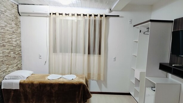 Quarto de hotel com duas camas, um guarda-roupa, uma TV e um pequeno frigorífico.