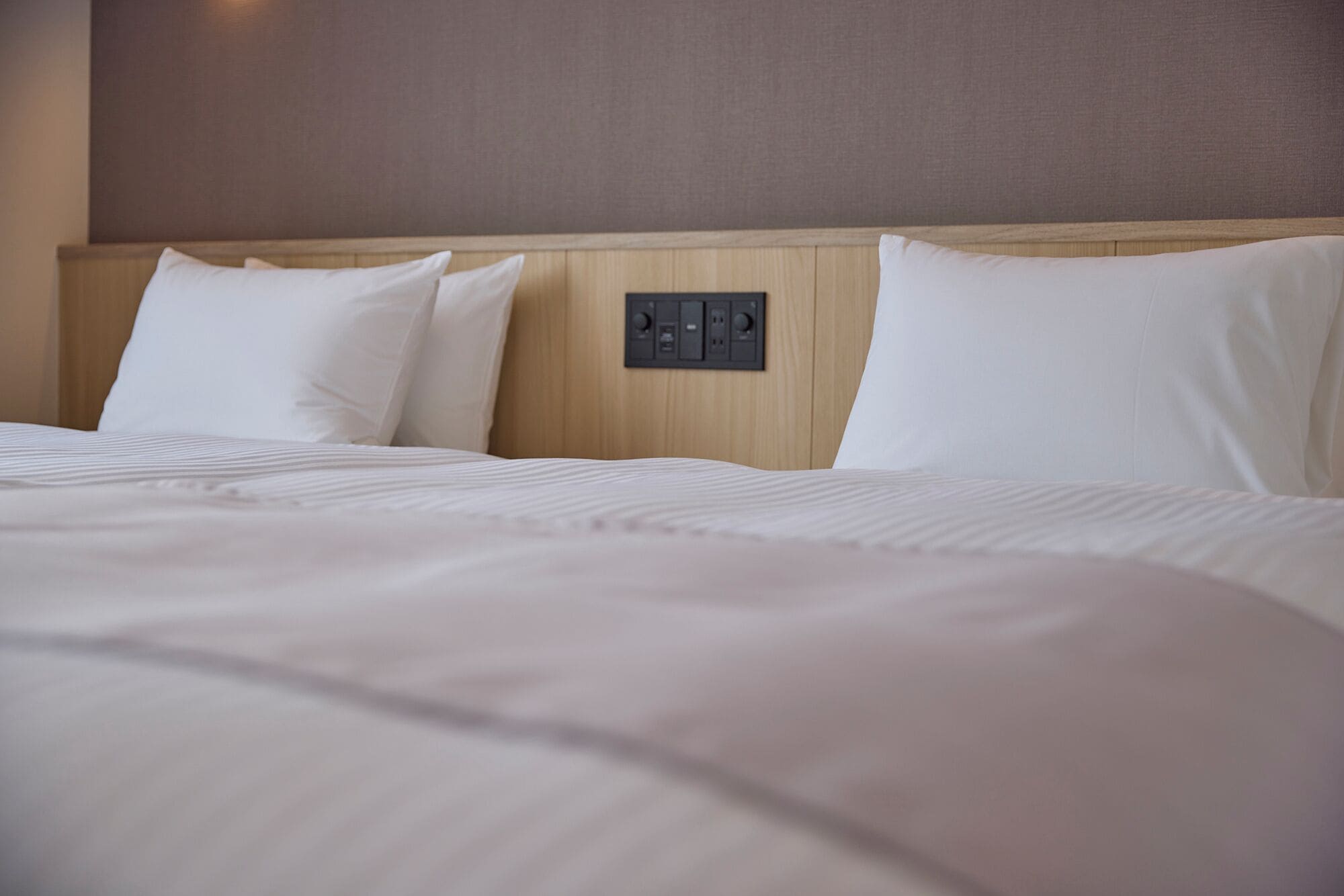Quarto de hotel com cama bem arrumada, cabeceira de madeira e painel de controle fixado na parede.