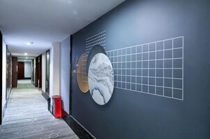 Um corredor com piso estampado, uma obra de arte na parede e uma lixeira.