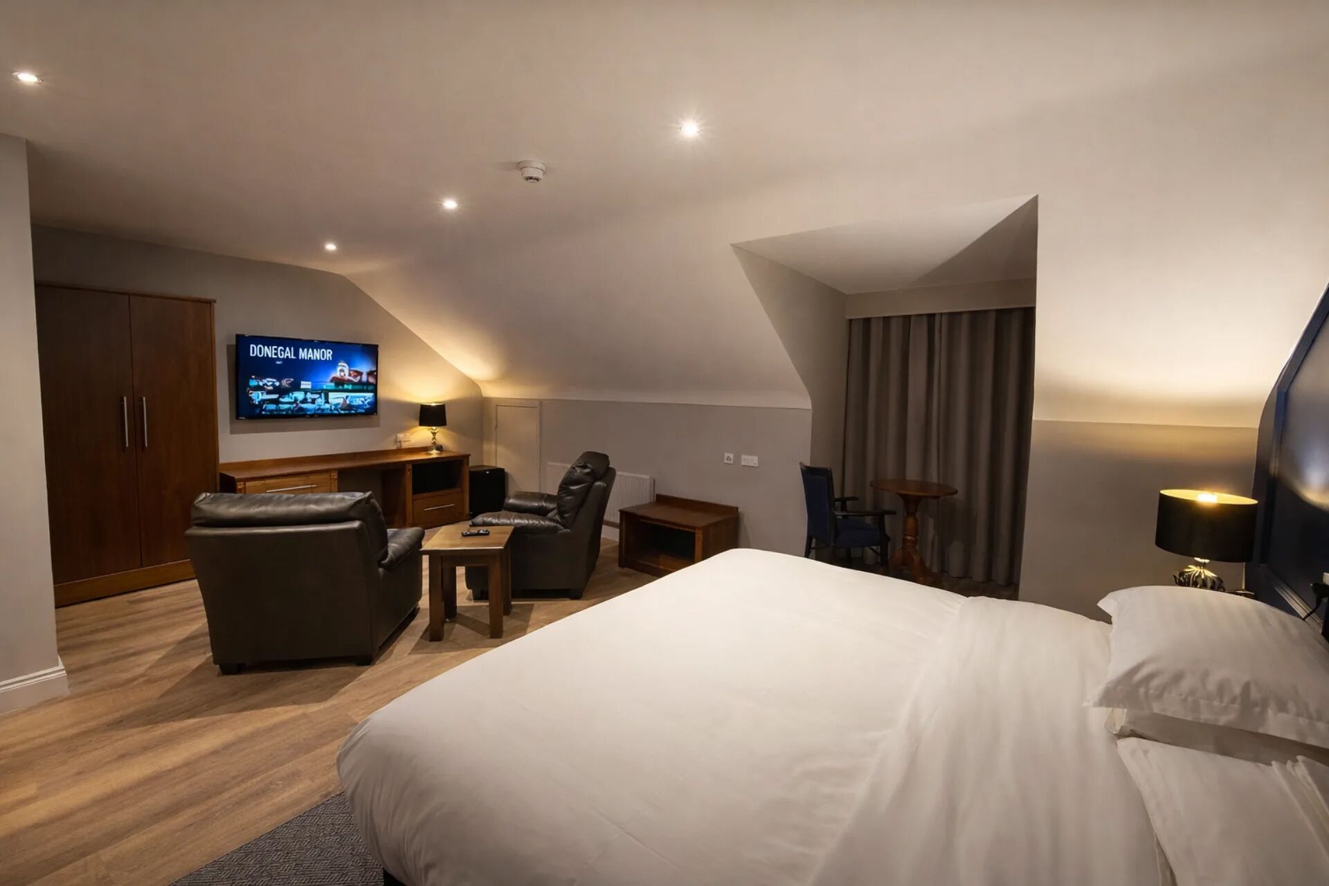 Quarto de hotel com uma cama grande, televisão, escrivaninha e área de estar.