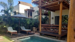 Uma área na piscina com espreguiçadeiras, um deck de madeira e uma estrutura com telhado de palha.