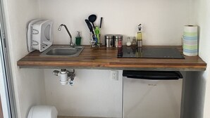 Uma cozinha compacta com prateleiras de madeira, uma pia, uma cafeteira e uma geladeira.