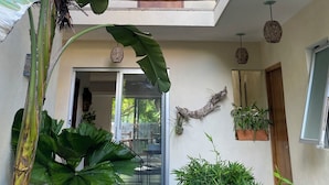 Um edifício com vários andares, uma varanda, plantas verdes grandes e uma porta que dá para o interior.