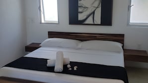 Quarto com uma cama grande, duas mesas de cabeceira, uma obra de arte na parede e duas janelas.