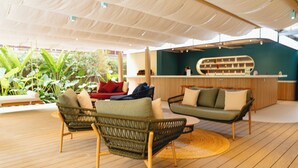 Uma área de convívio moderna com mobiliário de vime, um balcão de recepção e vista para o verde.