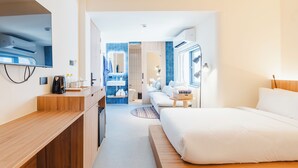 Quarto de hotel moderno com cama de madeira, uma mesa de escritório e um banheiro visível por uma porta aberta.