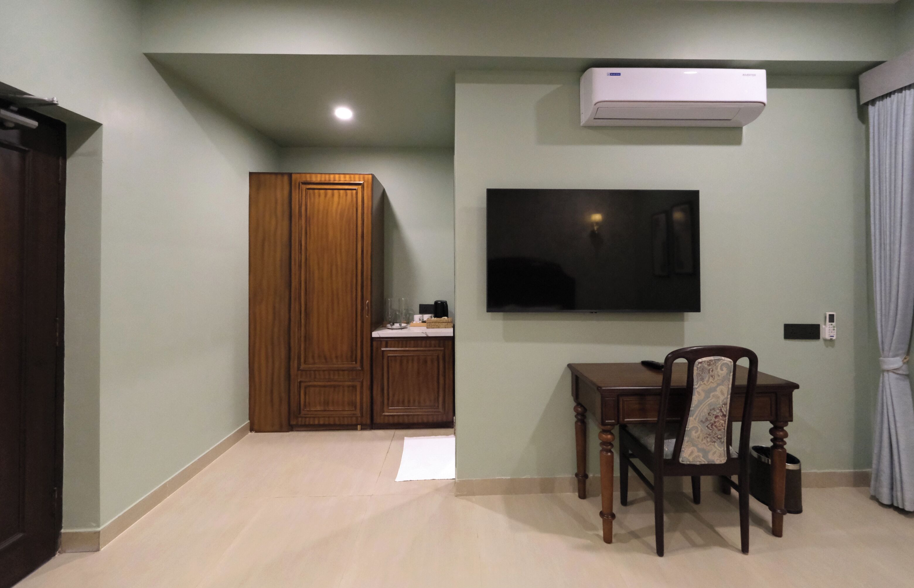 Quarto com guarda-roupa de madeira, mesa de jantar com cadeiras, televisão de ecrã plano na parede e unidade de ar condicionado.