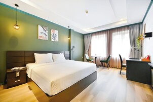 Quarto de hotel moderno com uma cama grande, uma escrivaninha, uma cadeira, uma mesinha e obras de arte nas paredes.