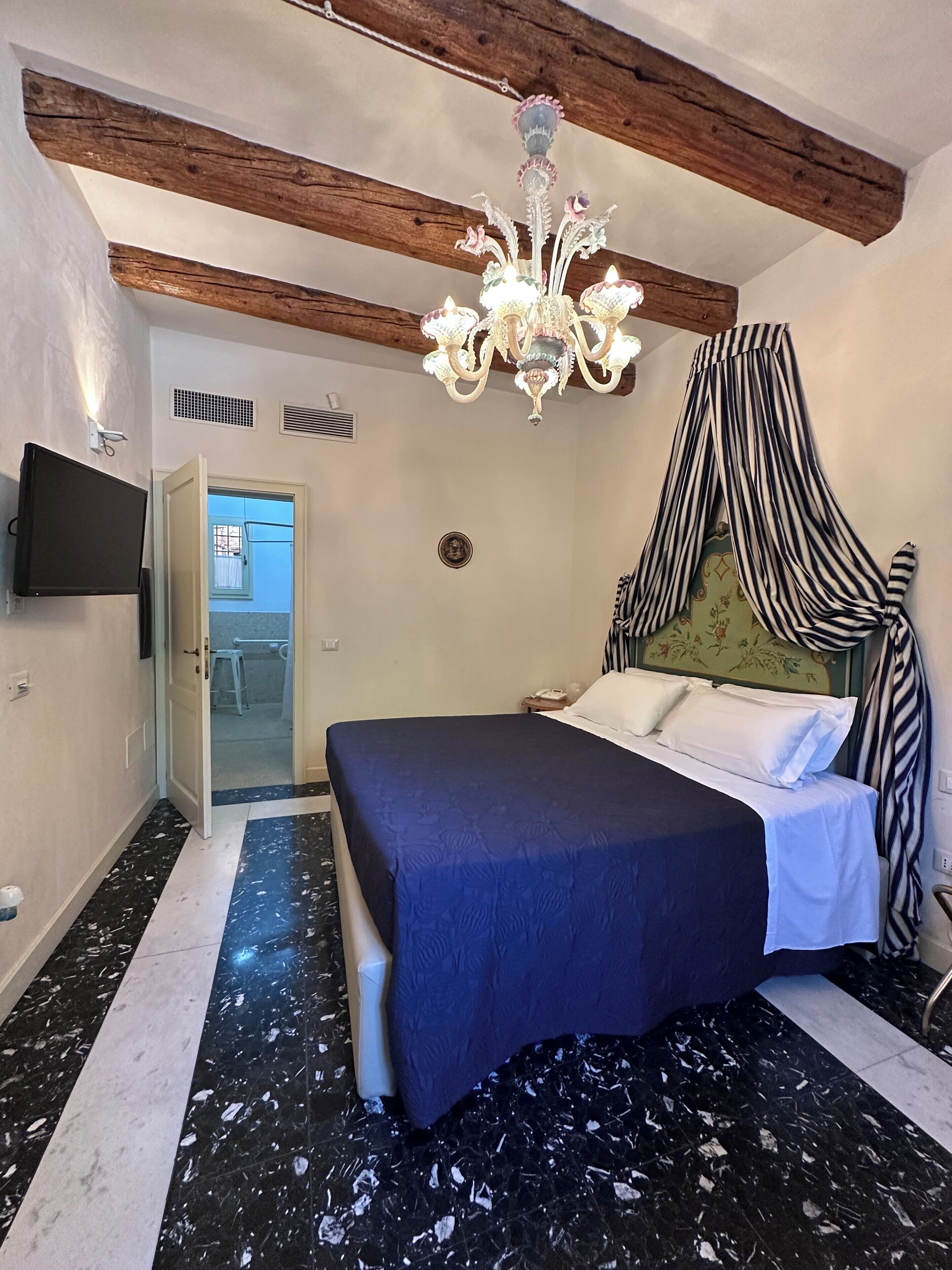 Quarto com cama, lustre, televisão e vista exterior.