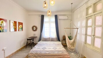 Um quarto com uma cama grande, uma escrivaninha, uma cadeira, um balanço e uma janela com cortinas.