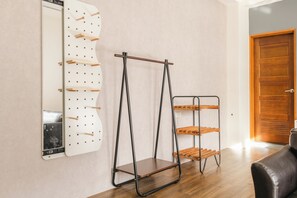 Quarto com piso de madeira, uma estante de cavilhas branca fixada na parede e uma cadeira de metal dobrável, além de uma porta de madeira.