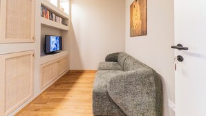 Quarto com estante embutida, televisão, sofá cinzento e um quadro na parede.