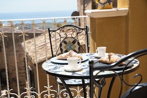 Uma mesa com um croissant e uma xícara numa varanda com vista para o mar.