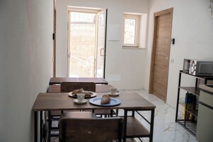 Uma área de refeições com uma mesa e cadeiras de madeira, uma janela pequena e uma porta.