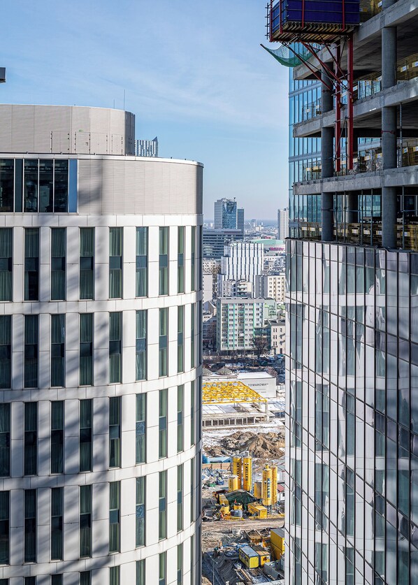 Um edifício moderno com fachada curva, grandes janelas e uma obra em construção abaixo.