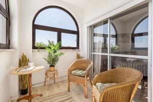 Uma varanda acolhedora com móveis de vime, uma planta em vaso e vista para a cidade.