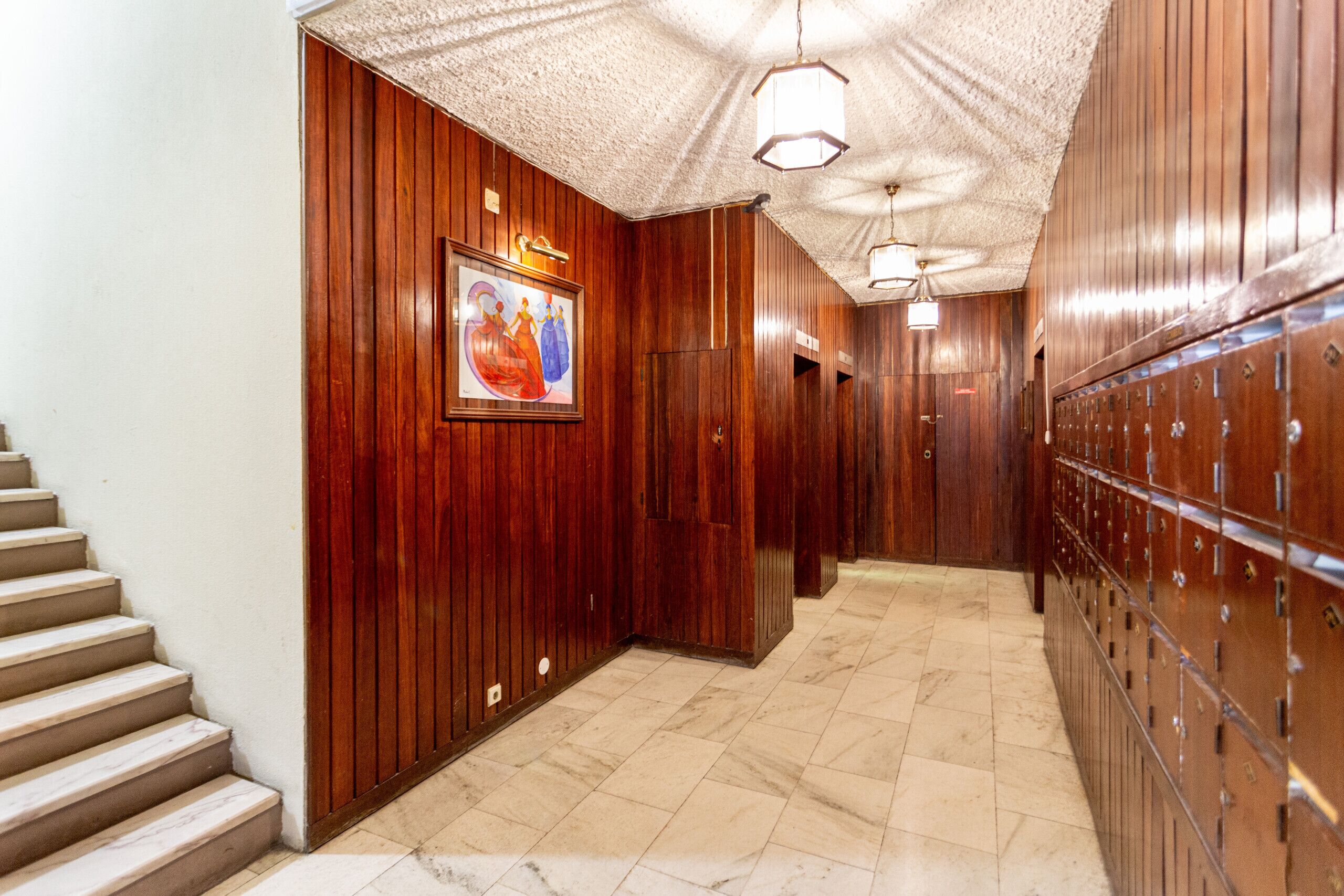 Um corredor com lambris de madeira, escadas, armários e um quadro pendurado na parede.