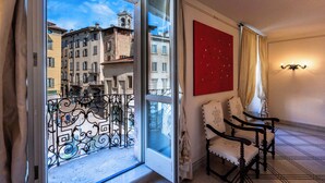 Quarto com varanda vista para a cidade, uma parede vermelha e duas poltronas estofadas.