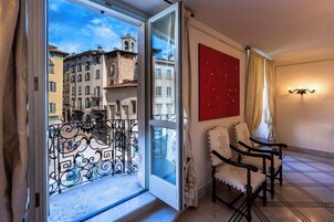 Quarto com varanda vista para a cidade, uma parede vermelha e duas poltronas estofadas.