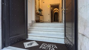 Uma entrada imponente com uma porta preta, degraus de mármore e um tapete de entrada com a inscrição "PALAZZO PORTA PICTA".