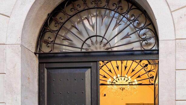 Uma entrada imponente com uma porta escura, um arco de metal decorativo e um candelabro.
