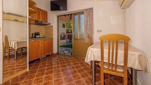 Uma cozinha compacta com armários de madeira, piso ladrilhado, mesa de jantar com cadeiras e uma televisão fixada na parede.