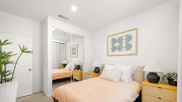 Quarto com cama, mesas de cabeceira, espelho e uma obra de arte na parede.