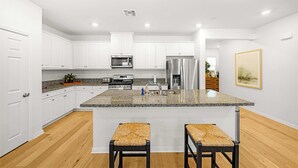 Cozinha moderna com armários brancos, bancadas de granito e eletrodomésticos de aço inoxidável, e dois banquetas.